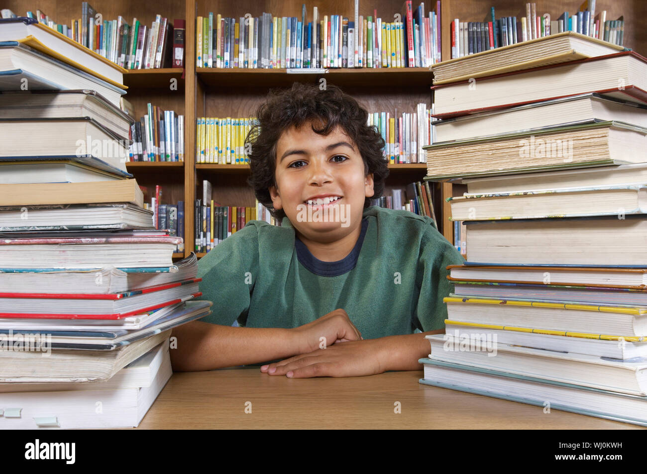 School boy sitting at desk with books in library, portrait Stock Photo ...