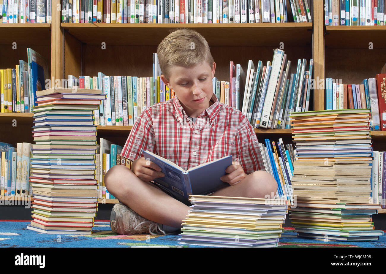 Boy sitting on the floor and reading book in library Stock Photo - Alamy