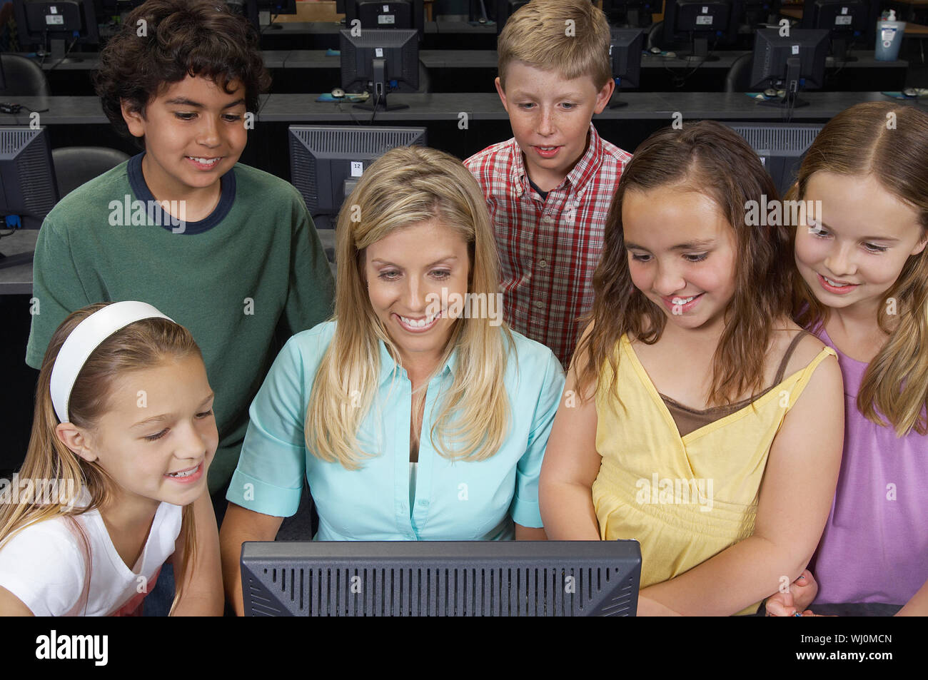 School children using computer with teacher in classroom Stock Photo ...