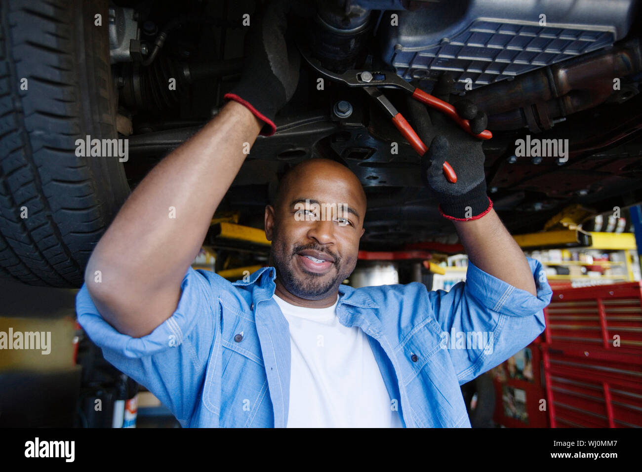 Portrait of a happy African American male mechanic repairing a lifted ...