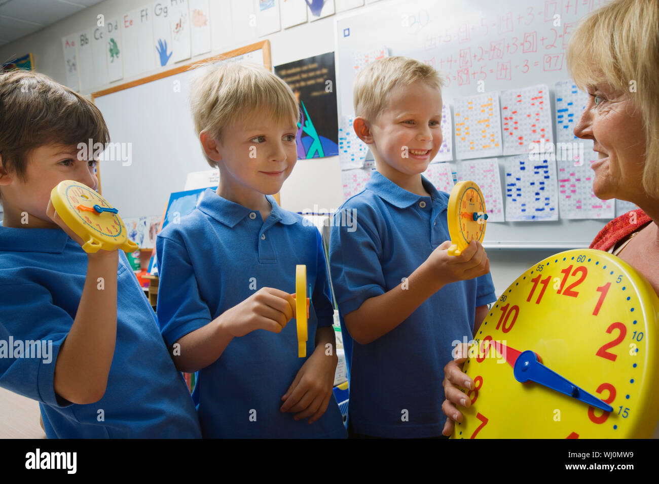 Three happy preadolescent boys showing yellow clock to the teacher in ...