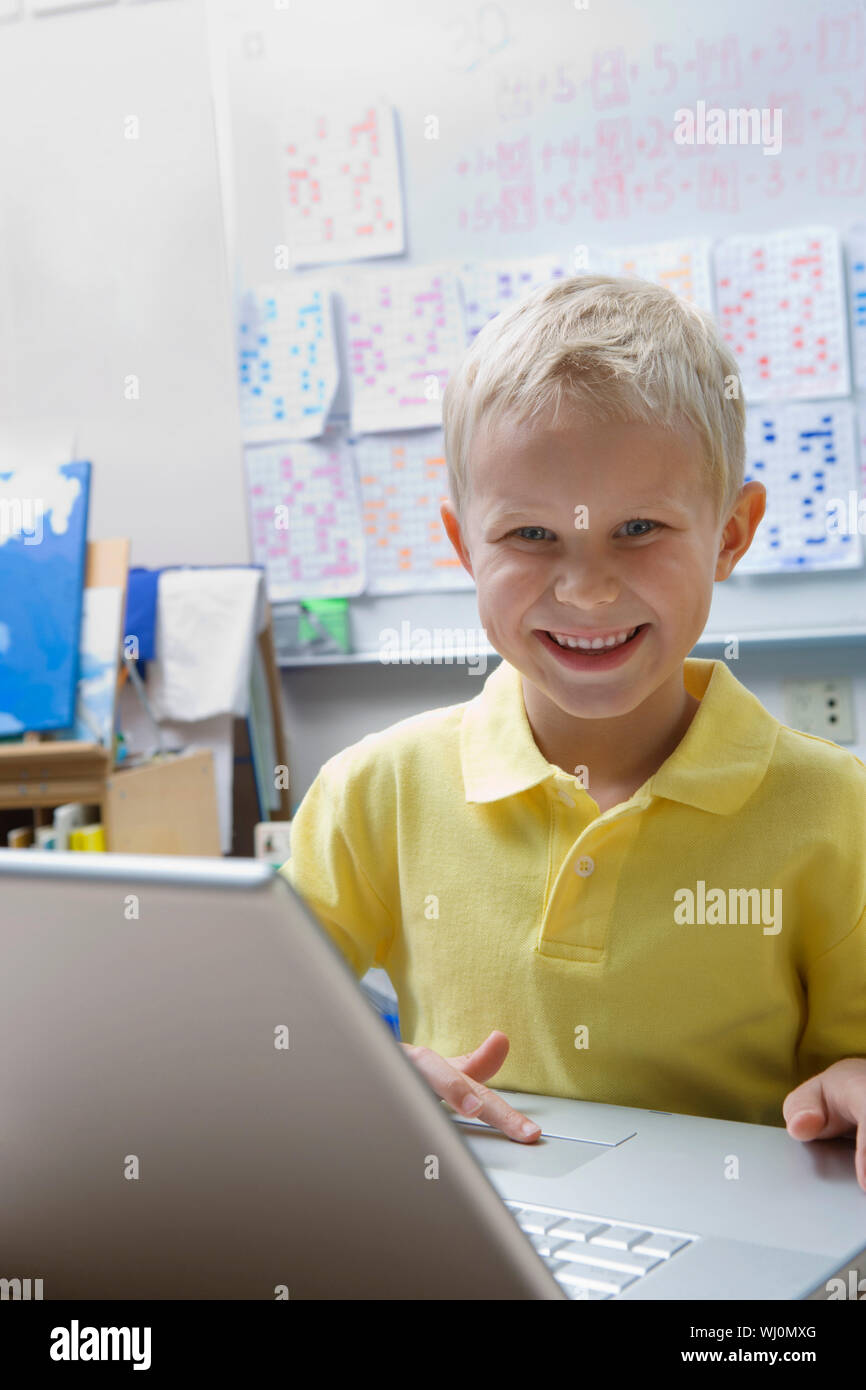 Portrait of a happy preadolescent boy using laptop against whiteboard ...