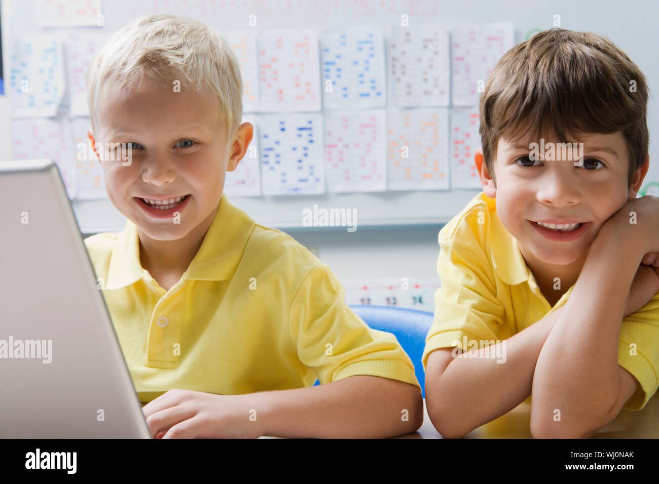 Portrait of happy boy using laptop sitting with friend against ...