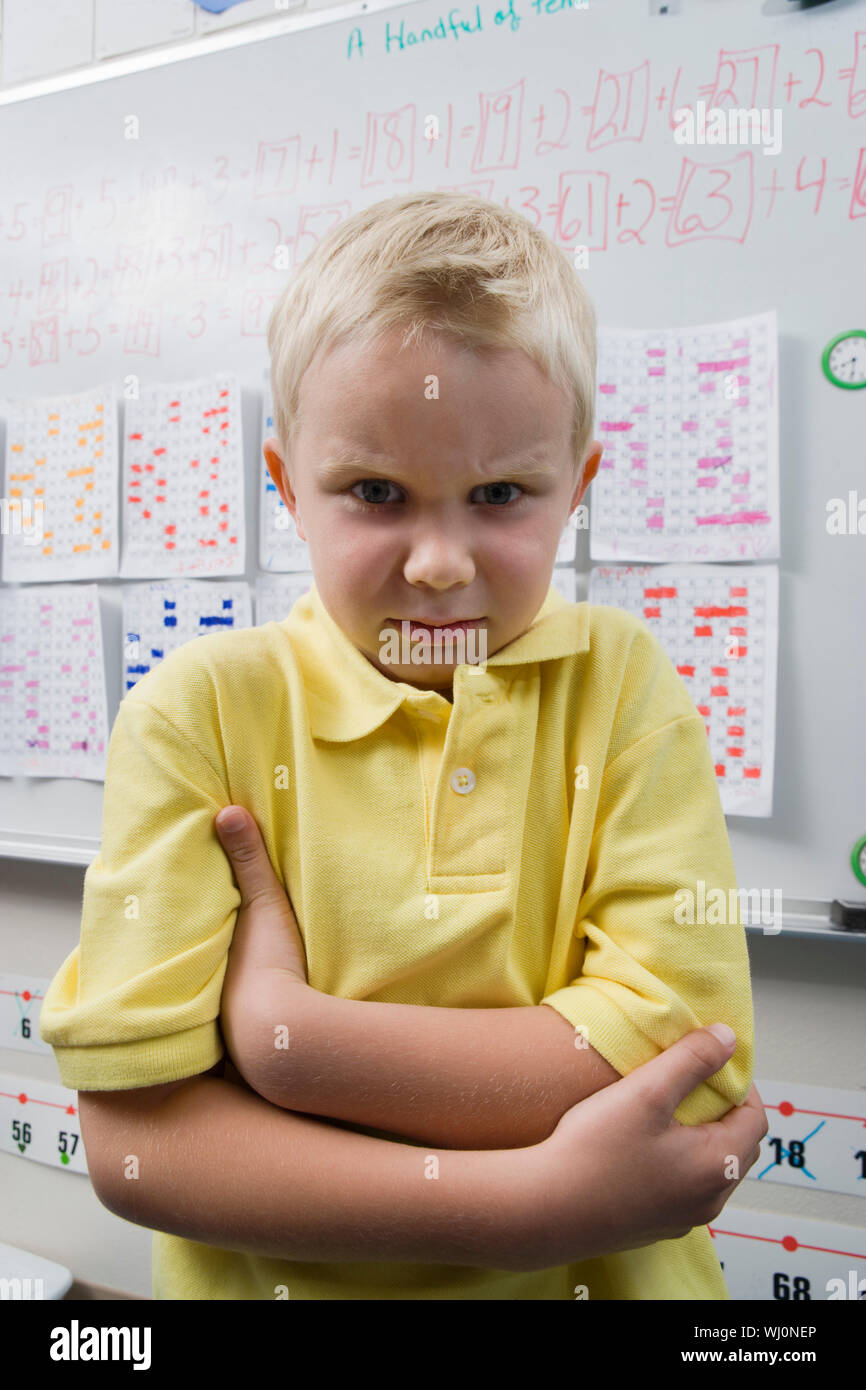 Portrait of an angry preadolescent student standing with hands folded ...