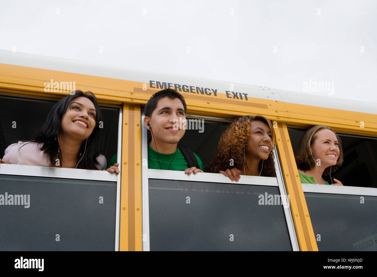 Low angle view of happy students looking through window of a school bus ...