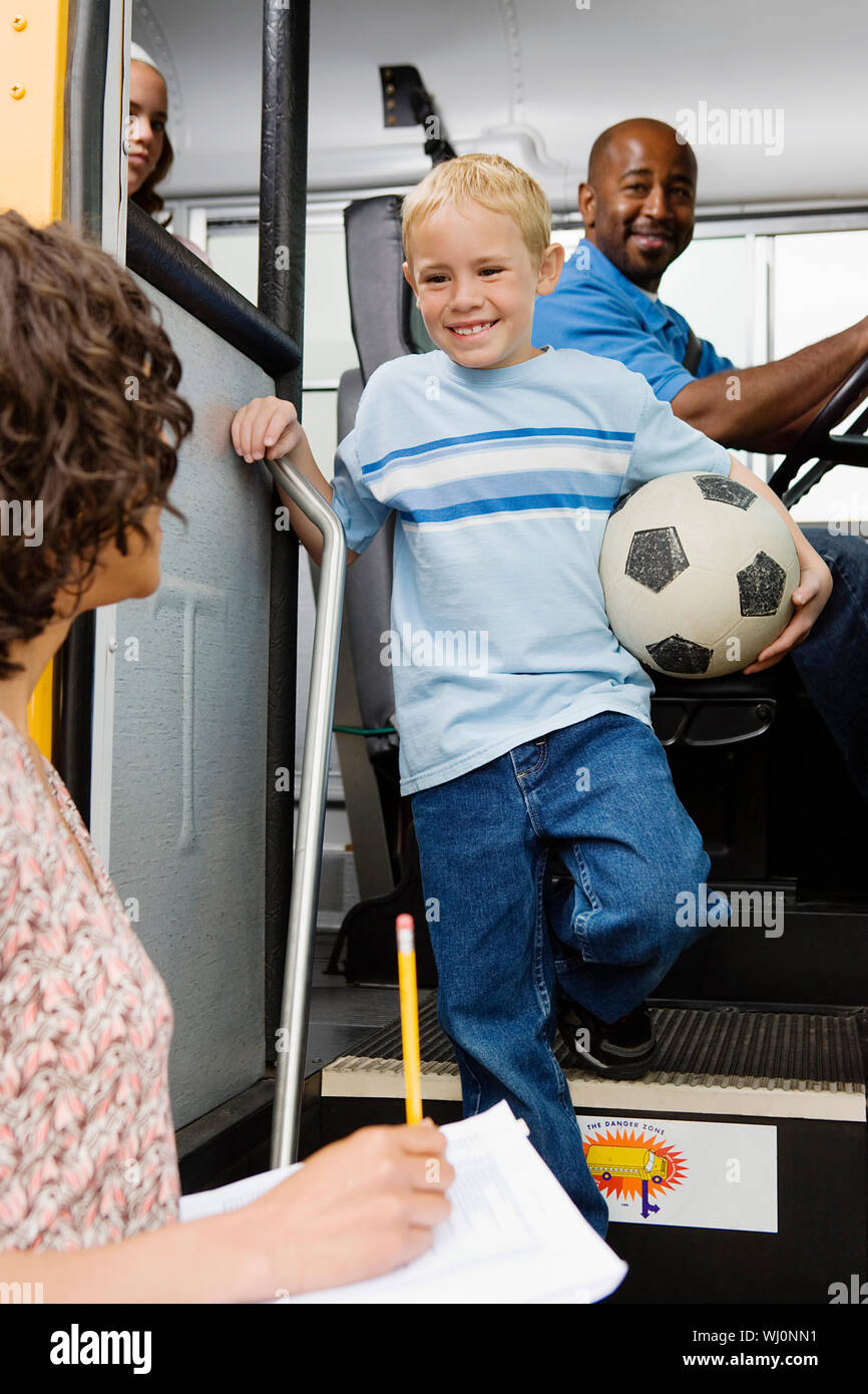 Little boy with a football getting down from school bus while looking ...