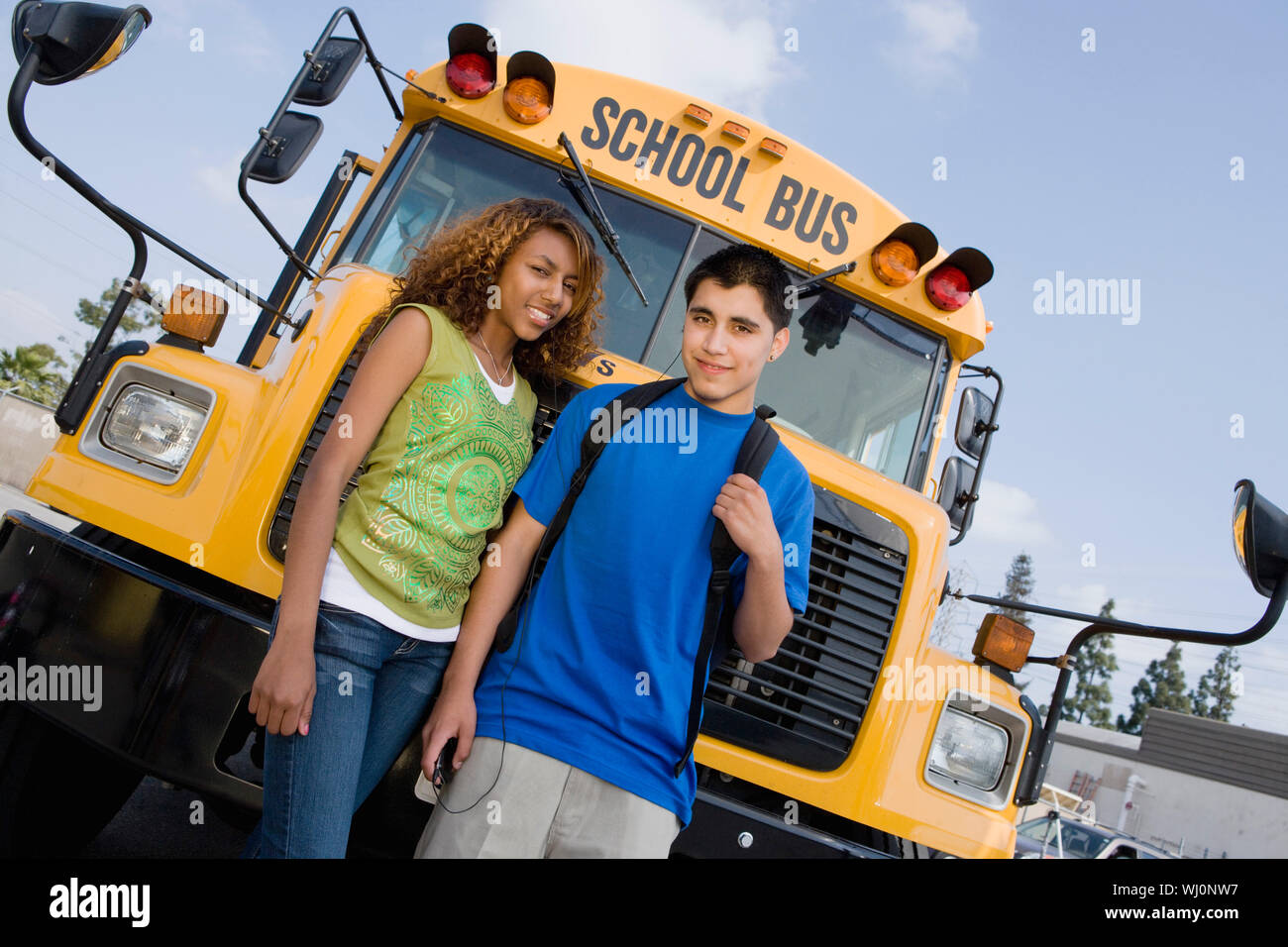 Tilt shot of happy friends standing together in front of school bus ...
