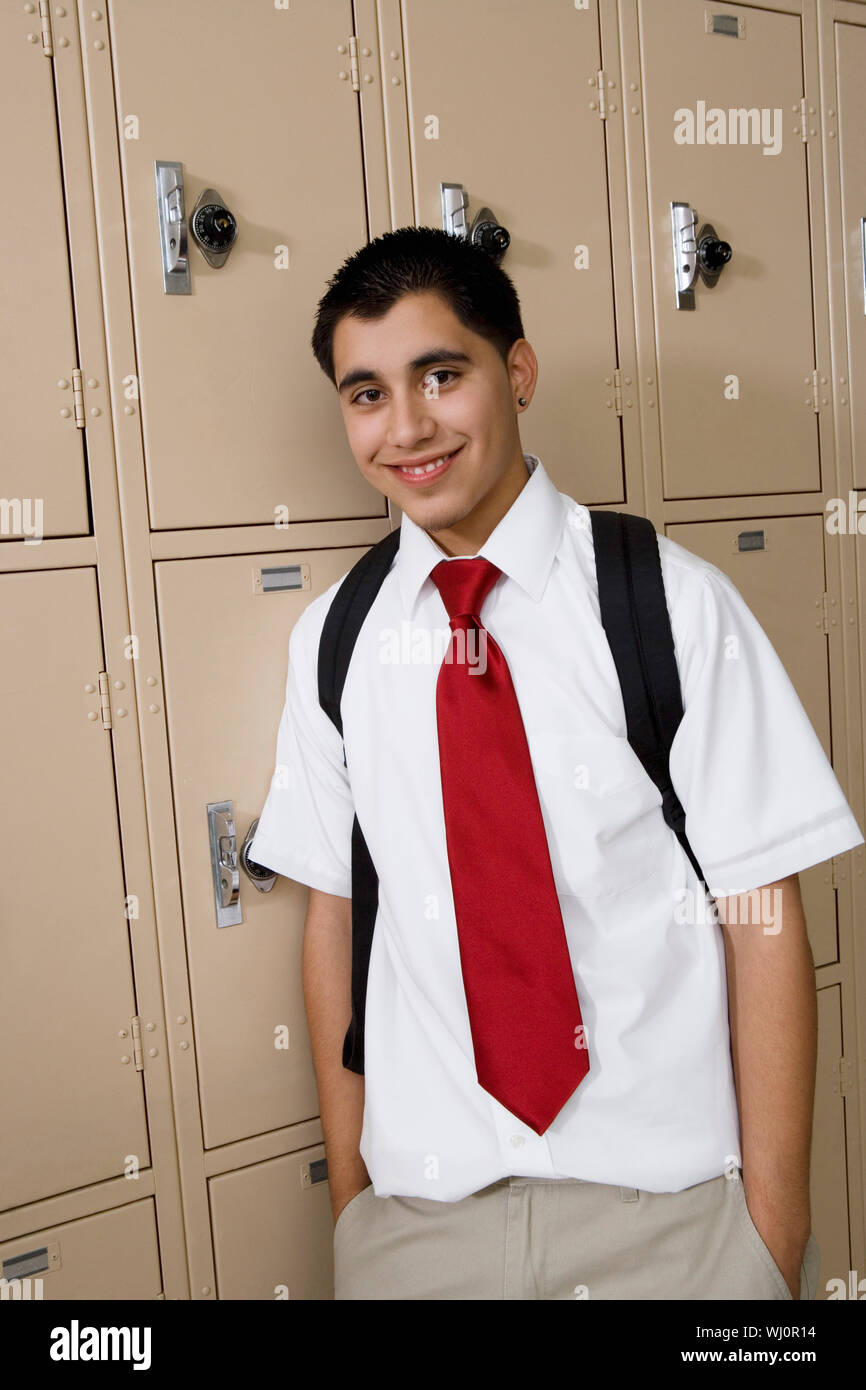 Portrait of a smart male student with backpack standing by the lockers ...