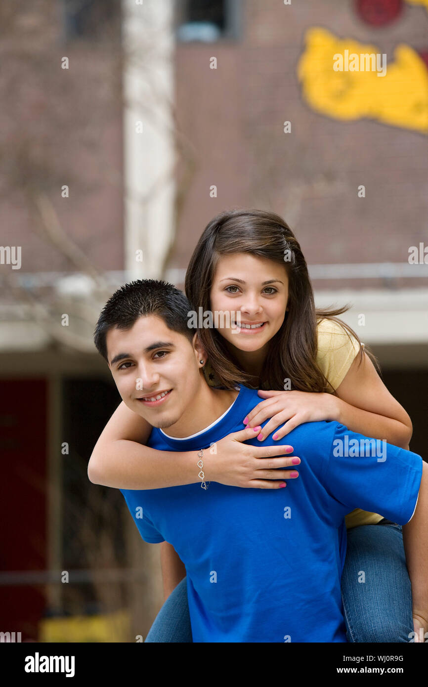 Portrait of young man giving piggyback ride to woman at collage campus ...