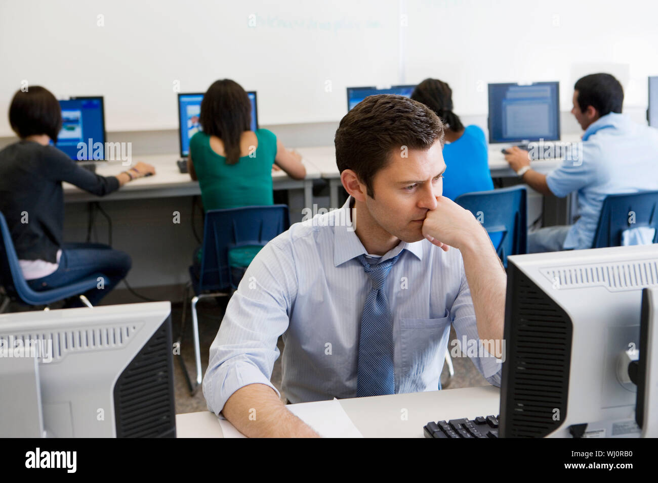 Professor working on computer in lab with students in the background ...