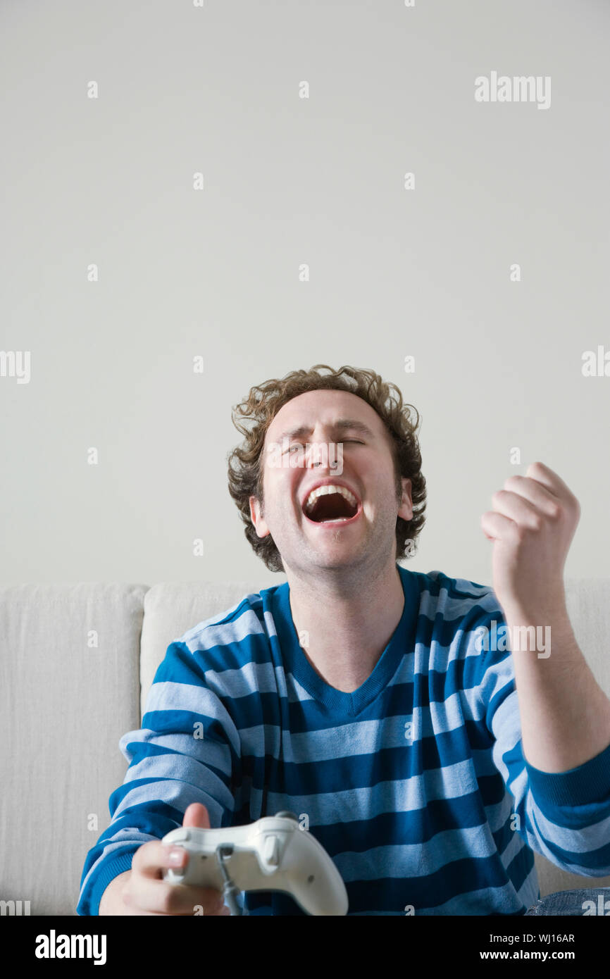 Laughing young man holding video game console on sofa Stock Photo - Alamy