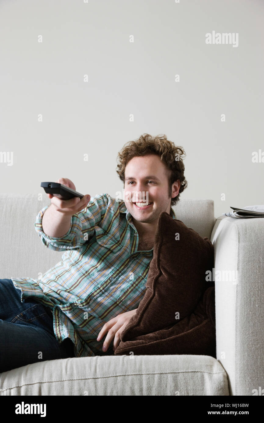 Happy young man on sofa with remote control and watching TV Stock Photo ...