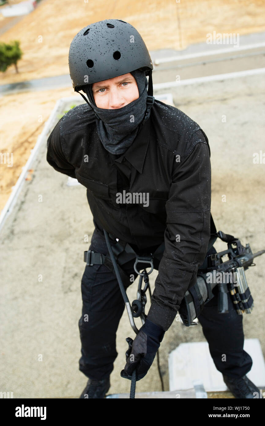 Middle aged armed man rappelling on building while aiming with gun ...