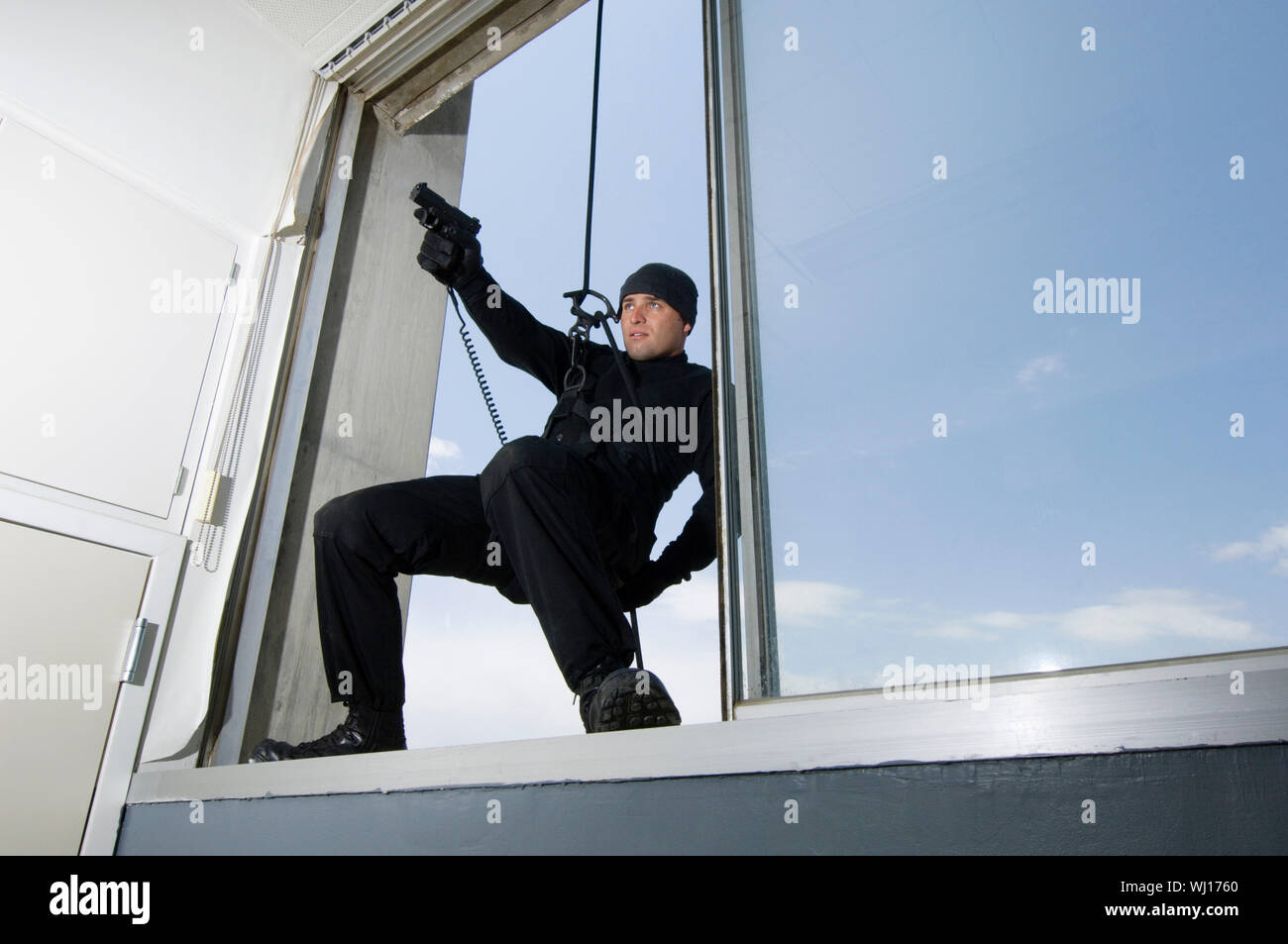 Middle aged armed man rappelling on building while aiming with gun ...