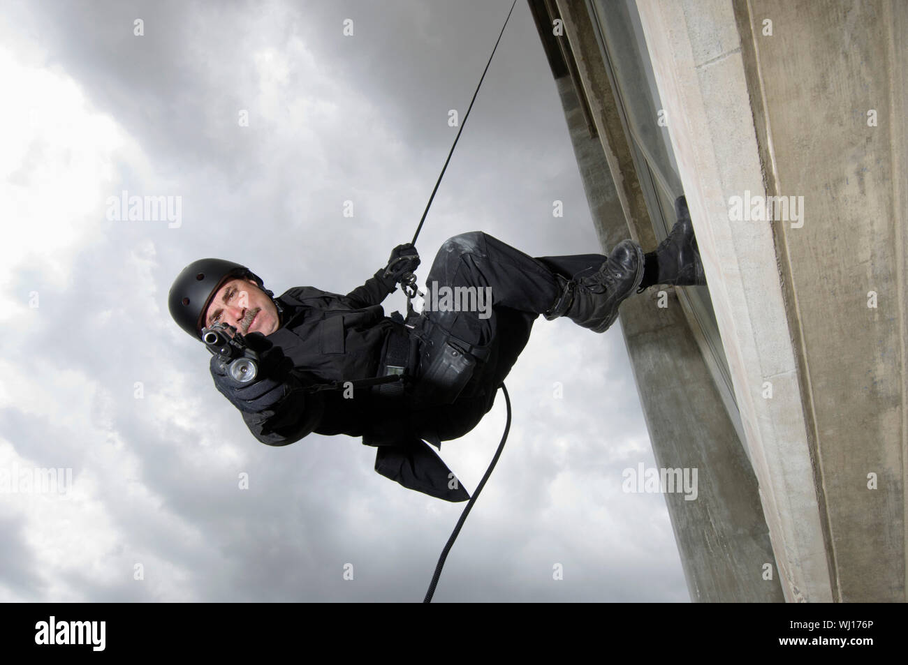 Full length of a trained man aiming gun while rappelling down the rope ...
