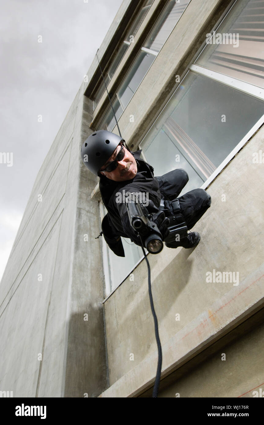 Full length of a trained man aiming gun while rappelling down the rope ...
