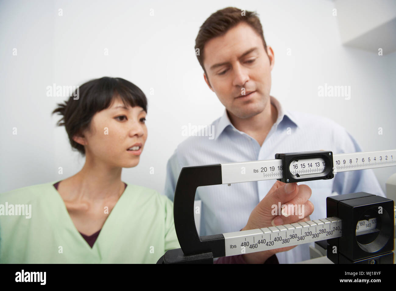 Man standing on weighing scales beside nurse in hospital Stock Photo ...