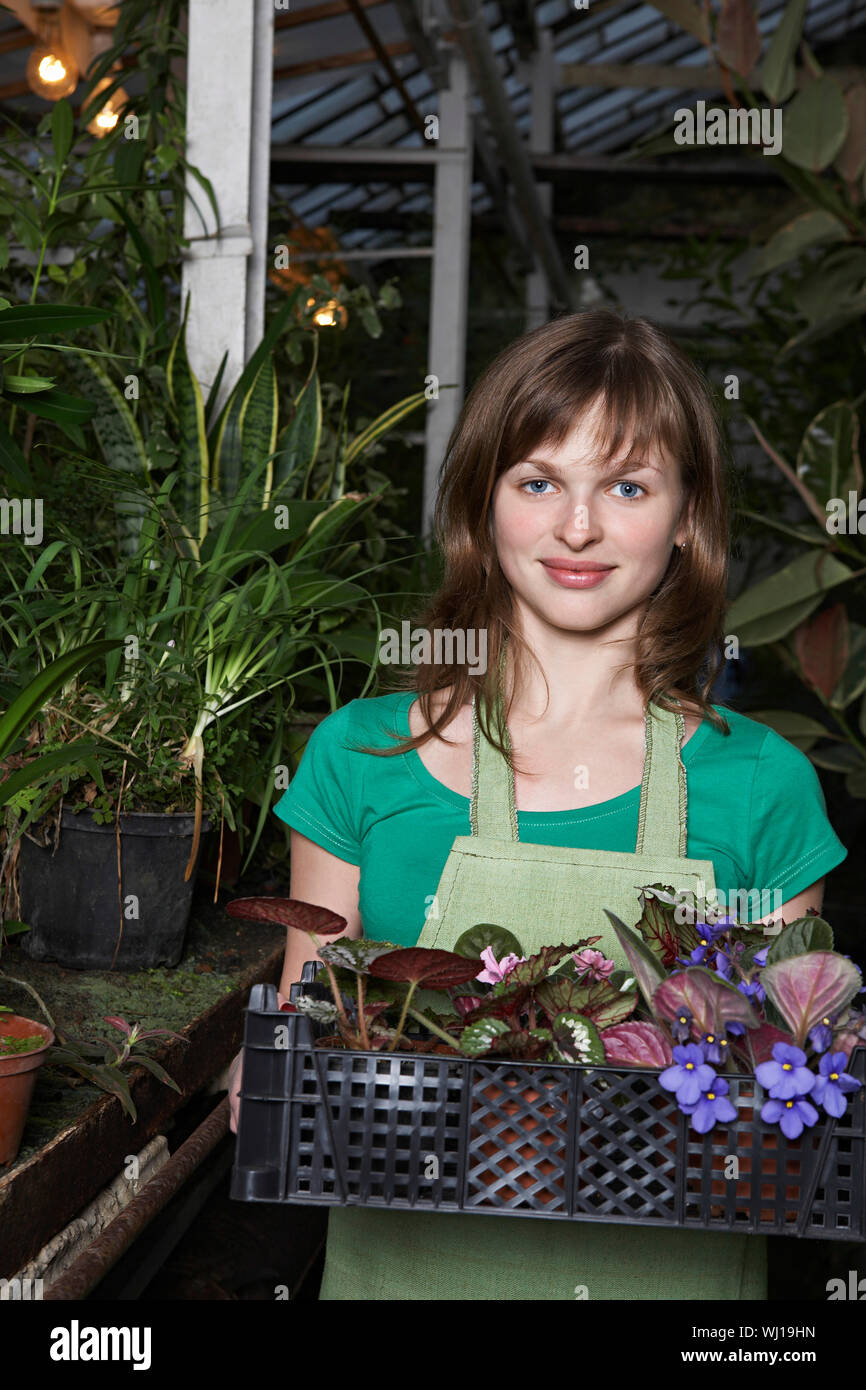 Portrait of beautiful botanist carrying crate full of flower plants at ...
