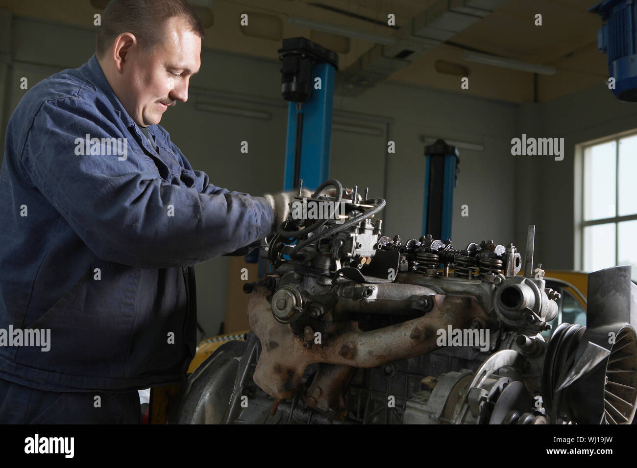 Side view of mechanic working on motor in garage Stock Photo - Alamy