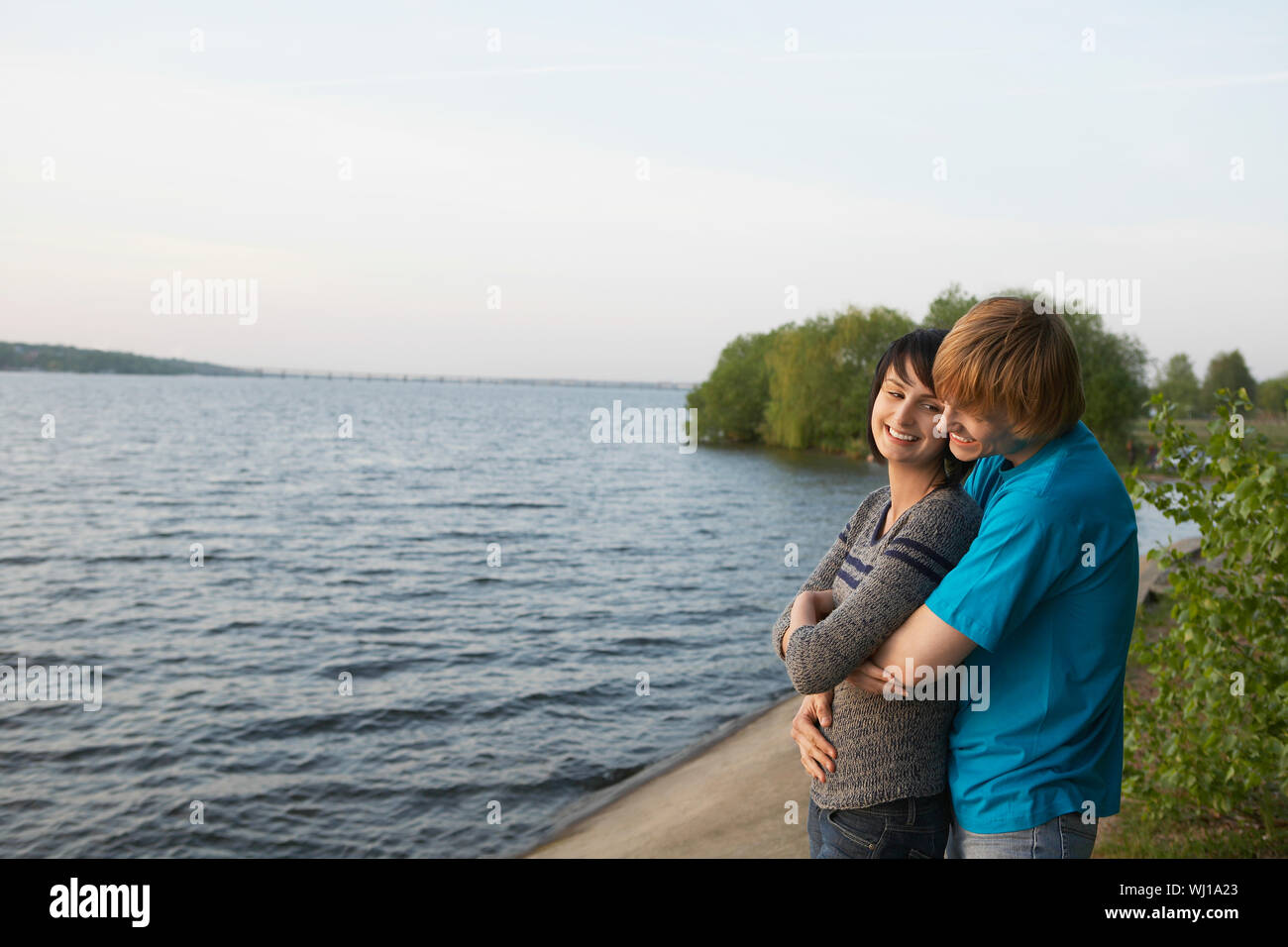Side view of a smiling young couple embracing on lakeshore Stock Photo ...