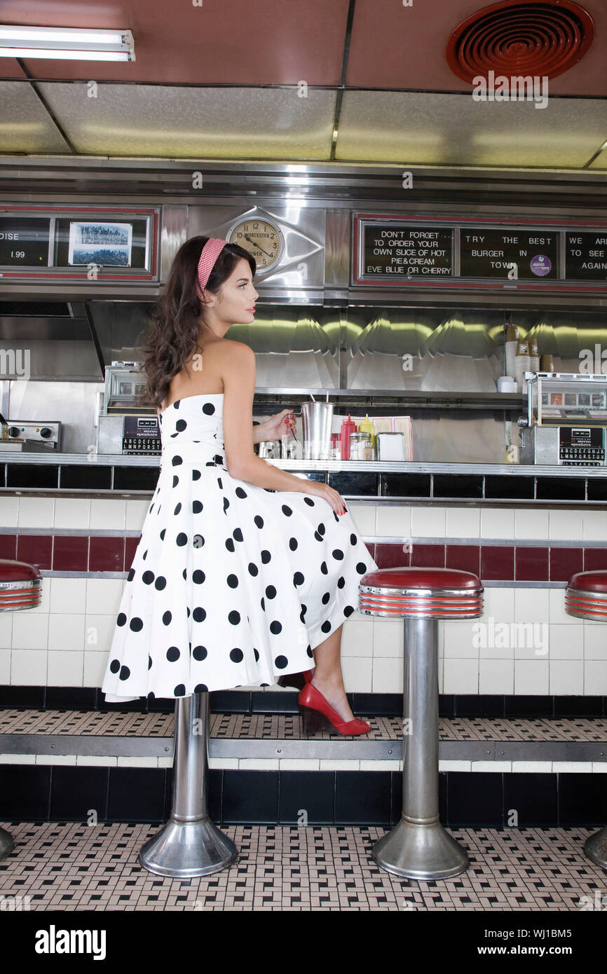 Full length side view of a young woman sitting at the diner counter ...