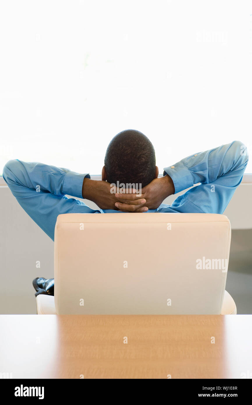 Rear View of a businessman sitting on chair with hands behind head ...