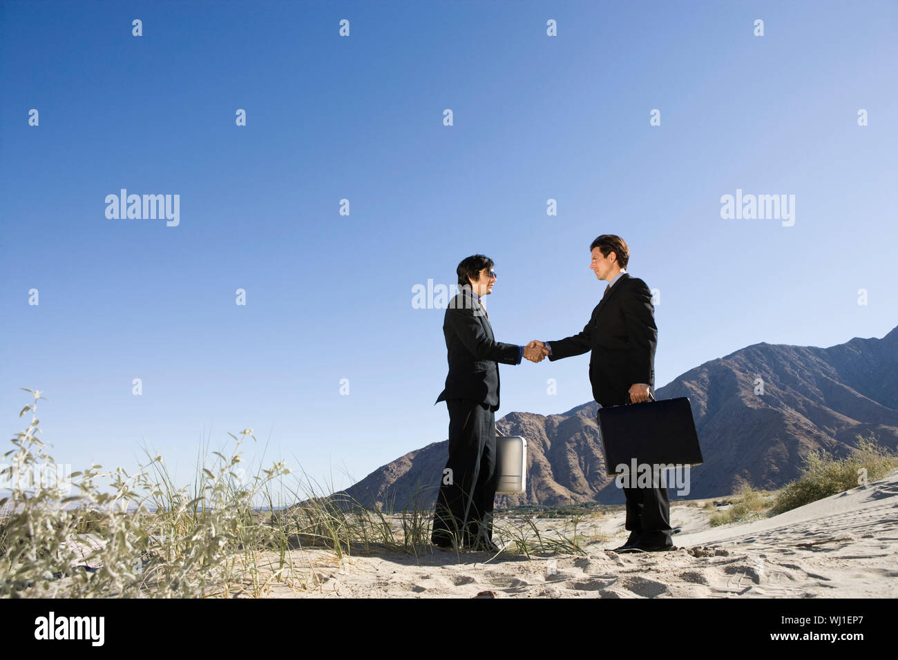 Full length of two businessmen shaking hands while holding briefcase in ...