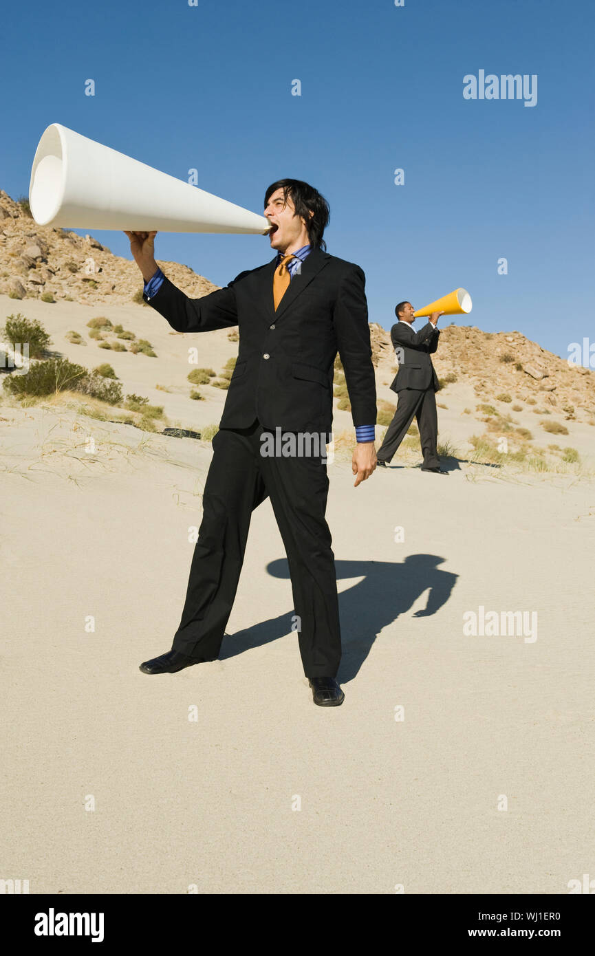 Two multiethnic businessmen shouting through bullhorn in desert Stock ...