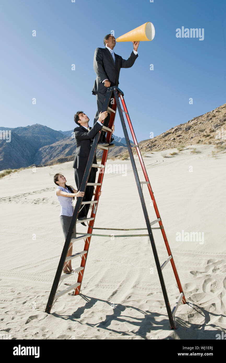 Businessman speaking through megaphone with colleagues standing on ...