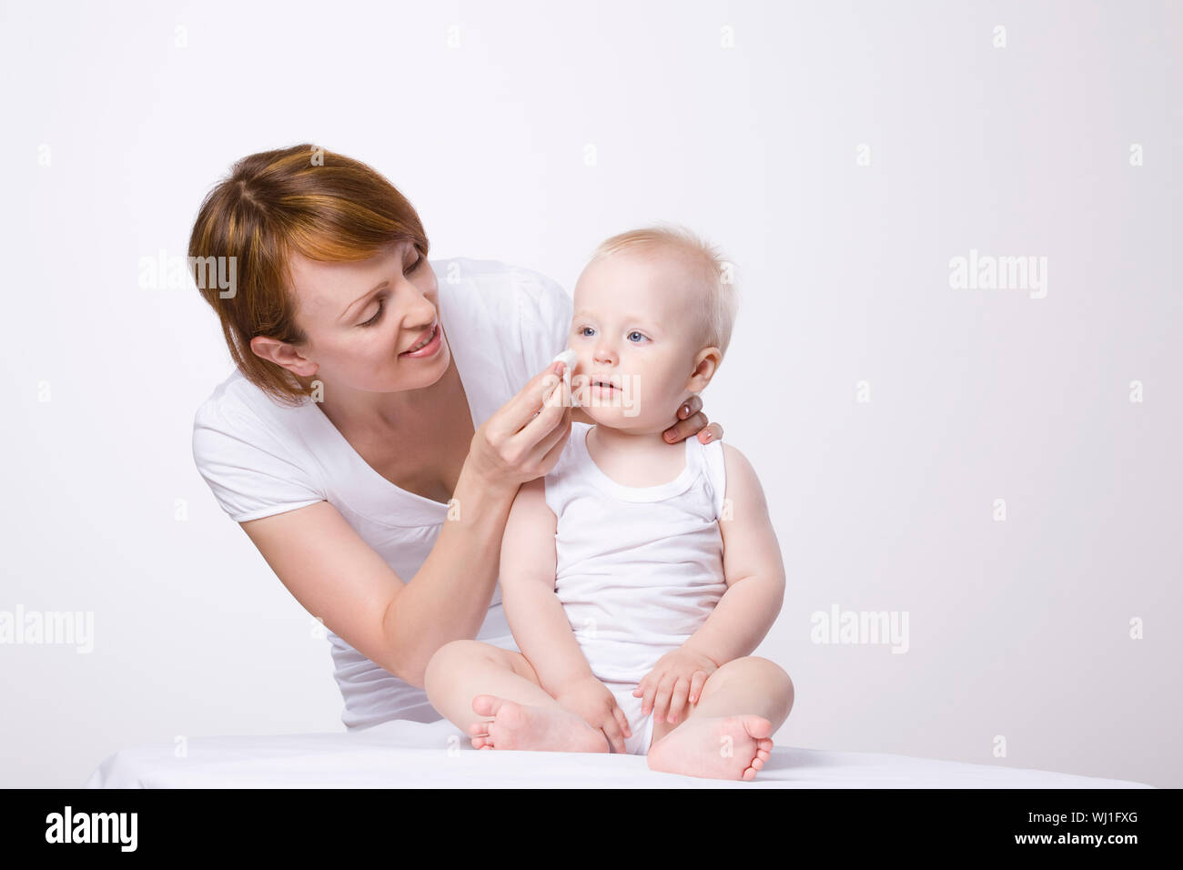 Young woman cleaning baby's face against white background Stock Photo ...