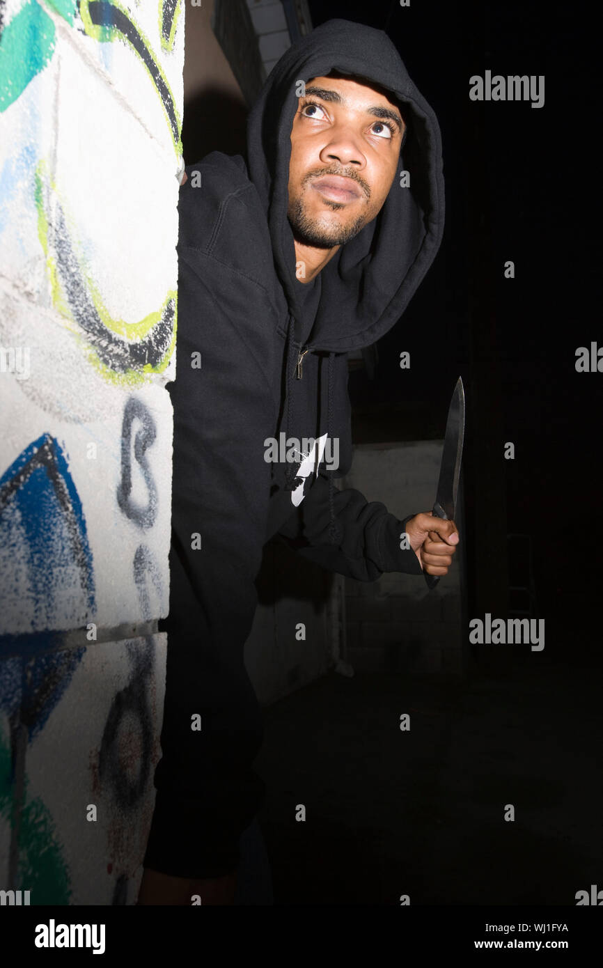 Robber with knife hiding behind corner Stock Photo - Alamy