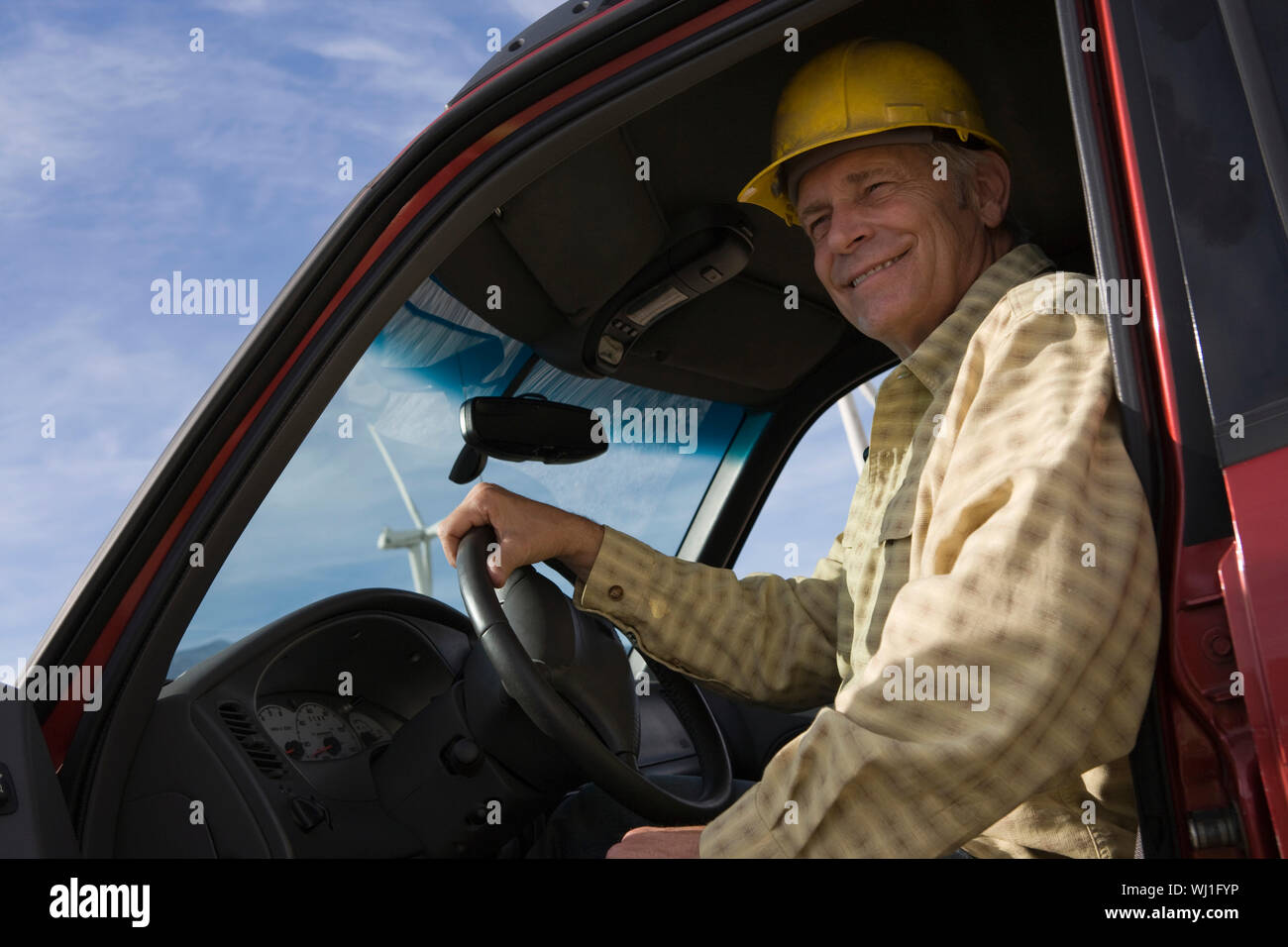 Happy senior male engineer sitting inside the car at windfarm against ...