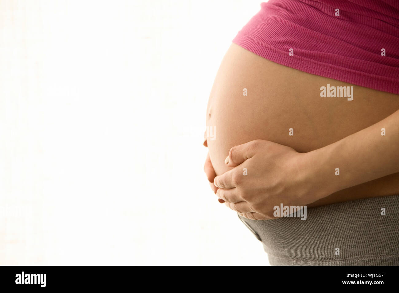 Side view midsection of a pregnant woman with hands holding tummy ...