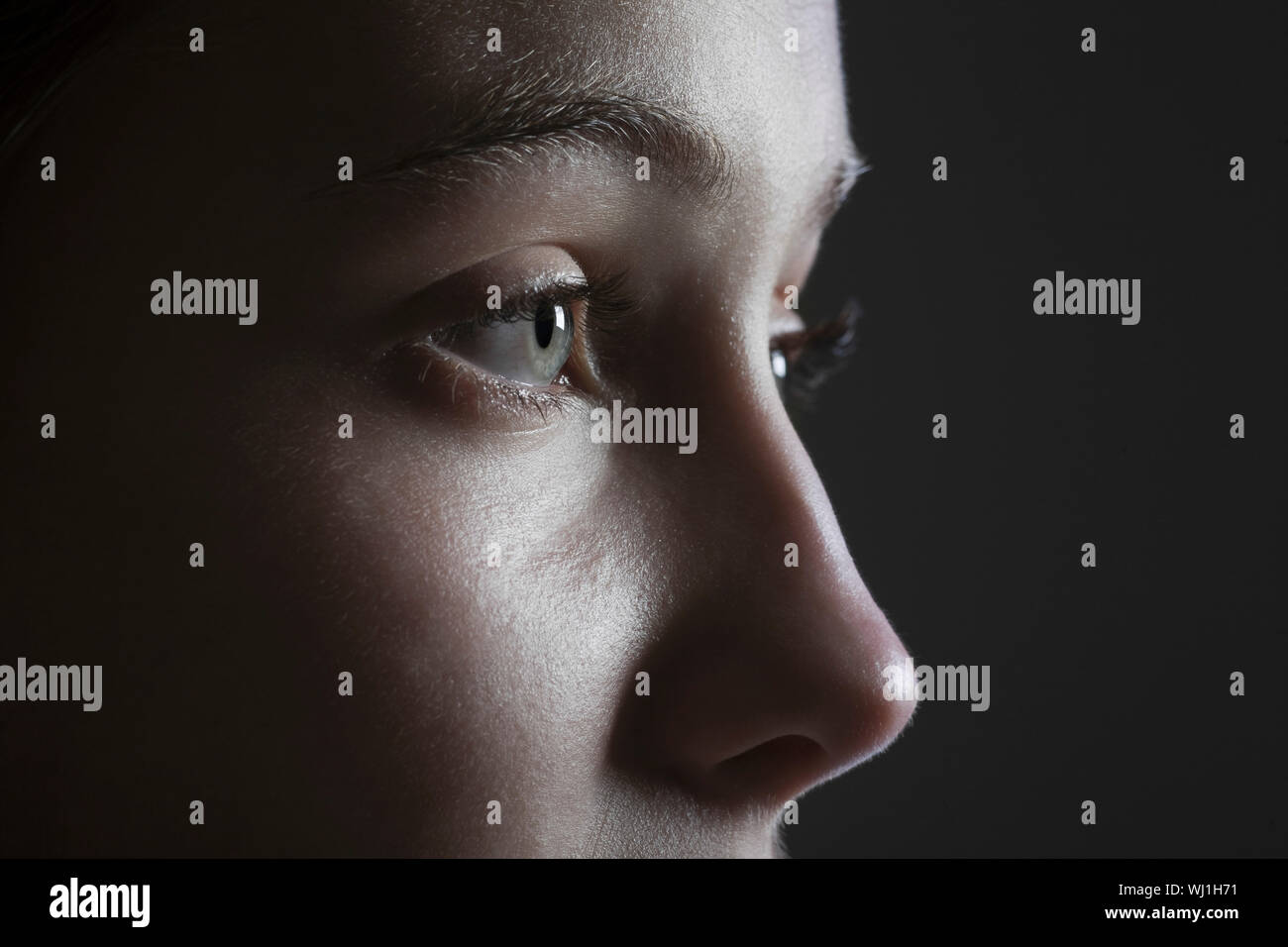 Closeup side view of a teenage girl looking away against black ...