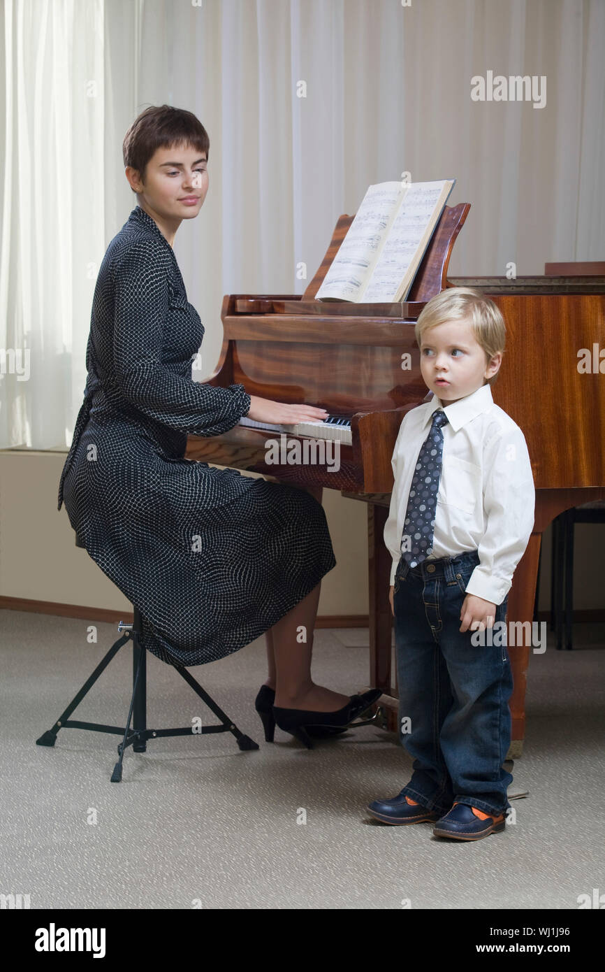 Little boy singing accompanied by teacher playing piano Stock Photo - Alamy