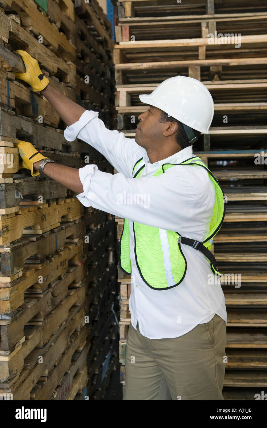 Side view of a man inspecting wooden pallets in distribution warehouse ...