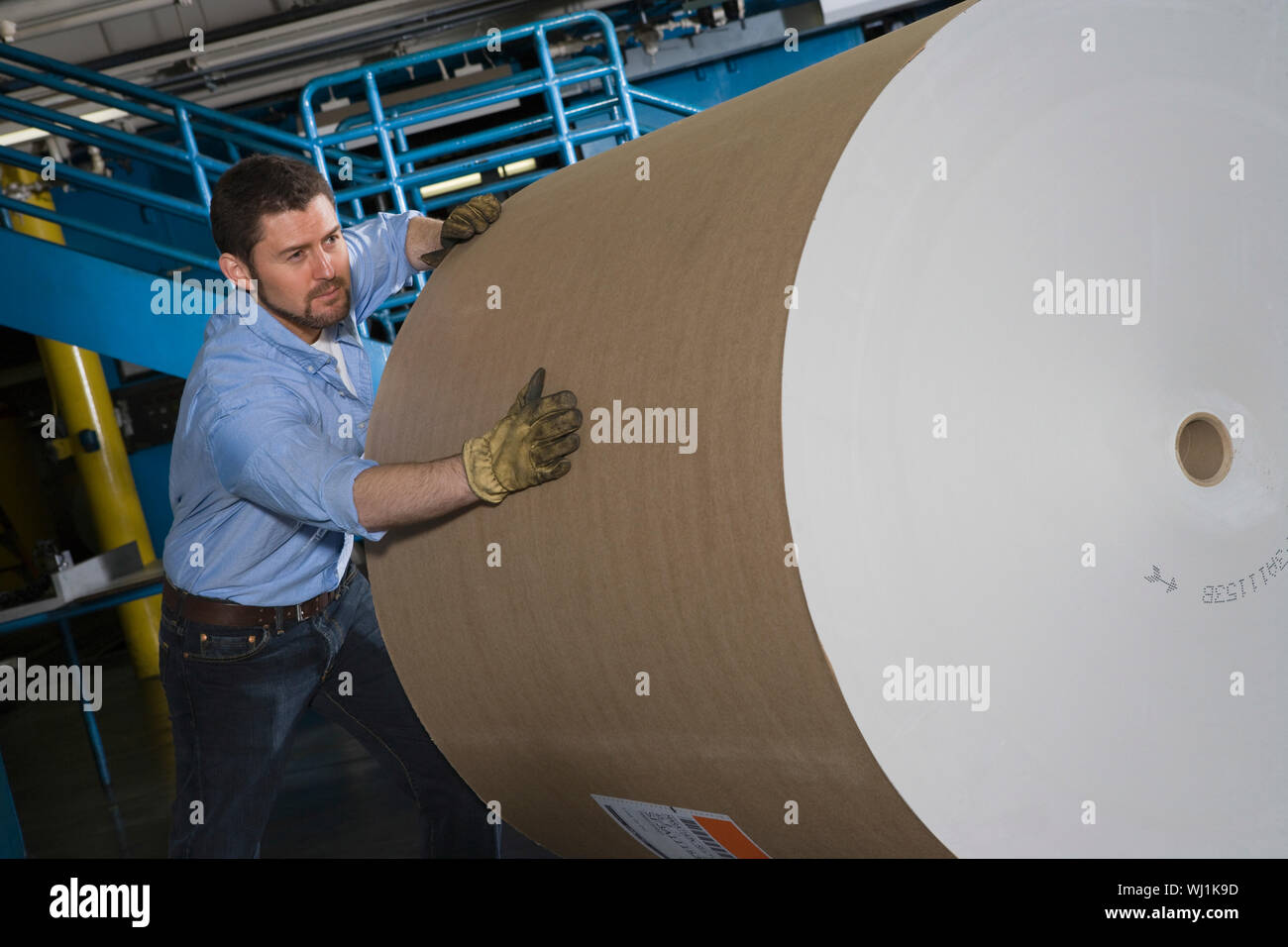 Man pushing huge roll of paper in newspaper factory Stock Photo - Alamy
