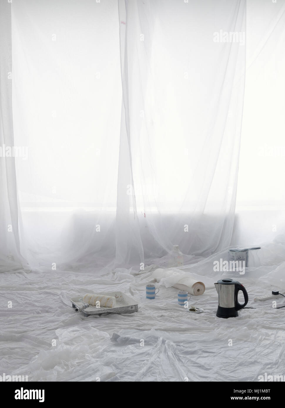 Empty room covered in dust sheets with kettle and painting supplies ...