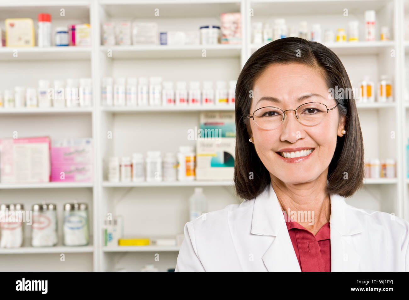 Portrait of a happy female pharmacist standing with hands folded at ...