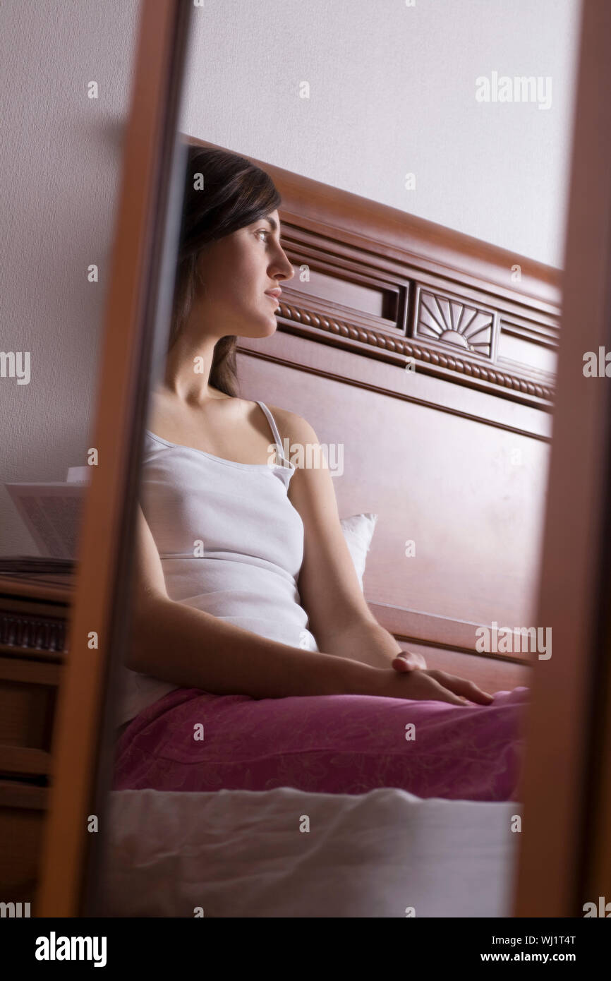 Thoughtful young woman reflecting in mirror while sitting on bed Stock ...