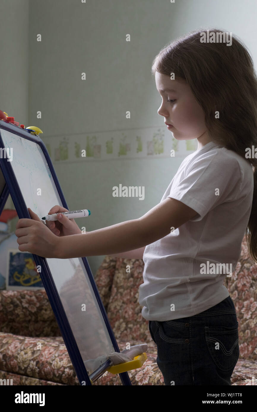 Side view of a little girl drawing on plastic board at home Stock Photo ...