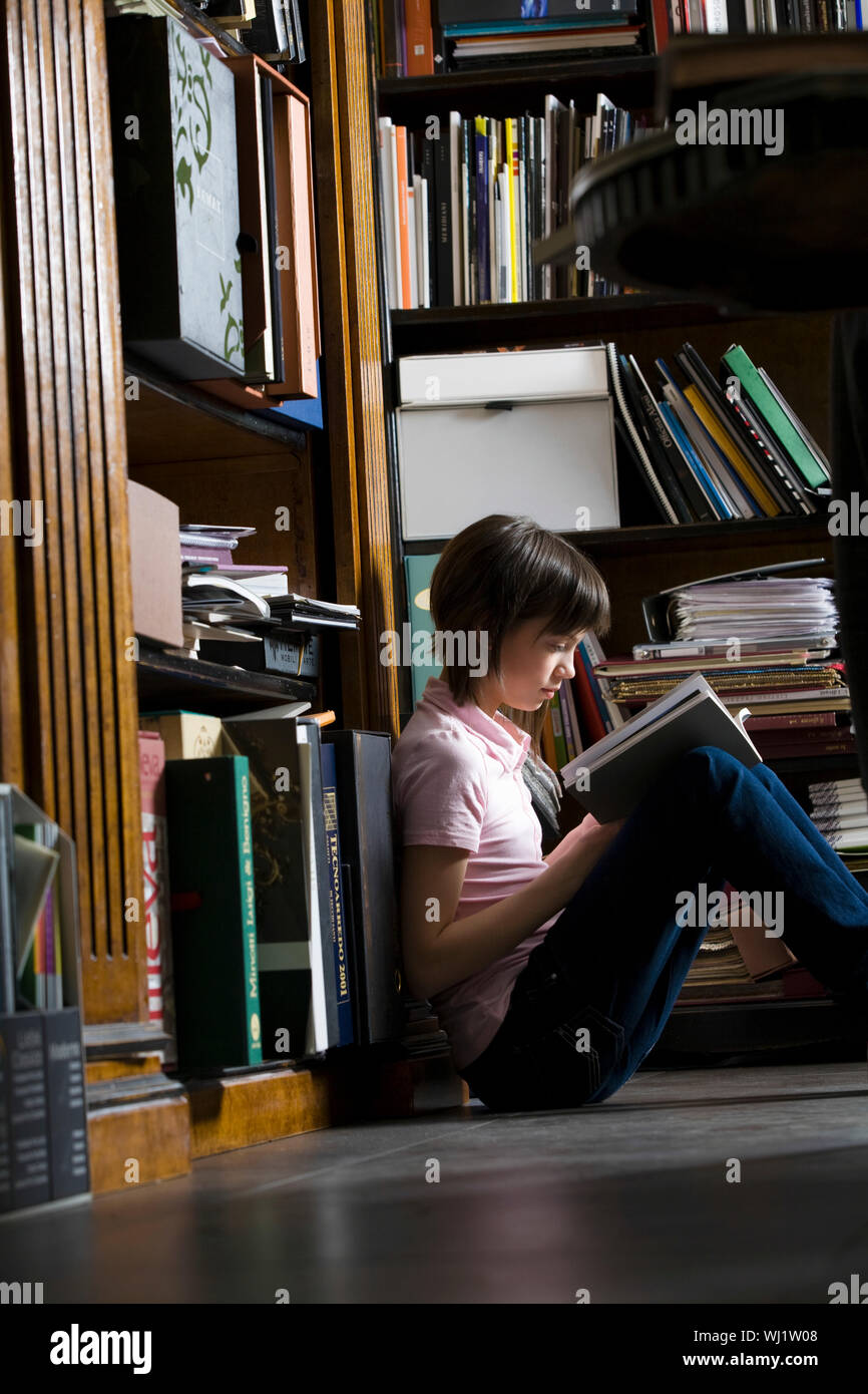 Side view of a young girl reading a book at the library Stock Photo - Alamy