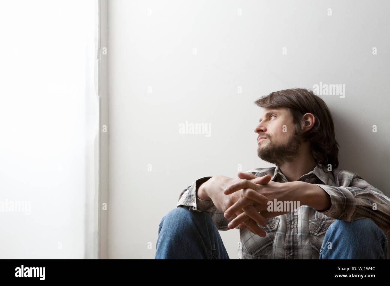 Man Siting With Hands Clasped Against Wall Stock Photo - Alamy