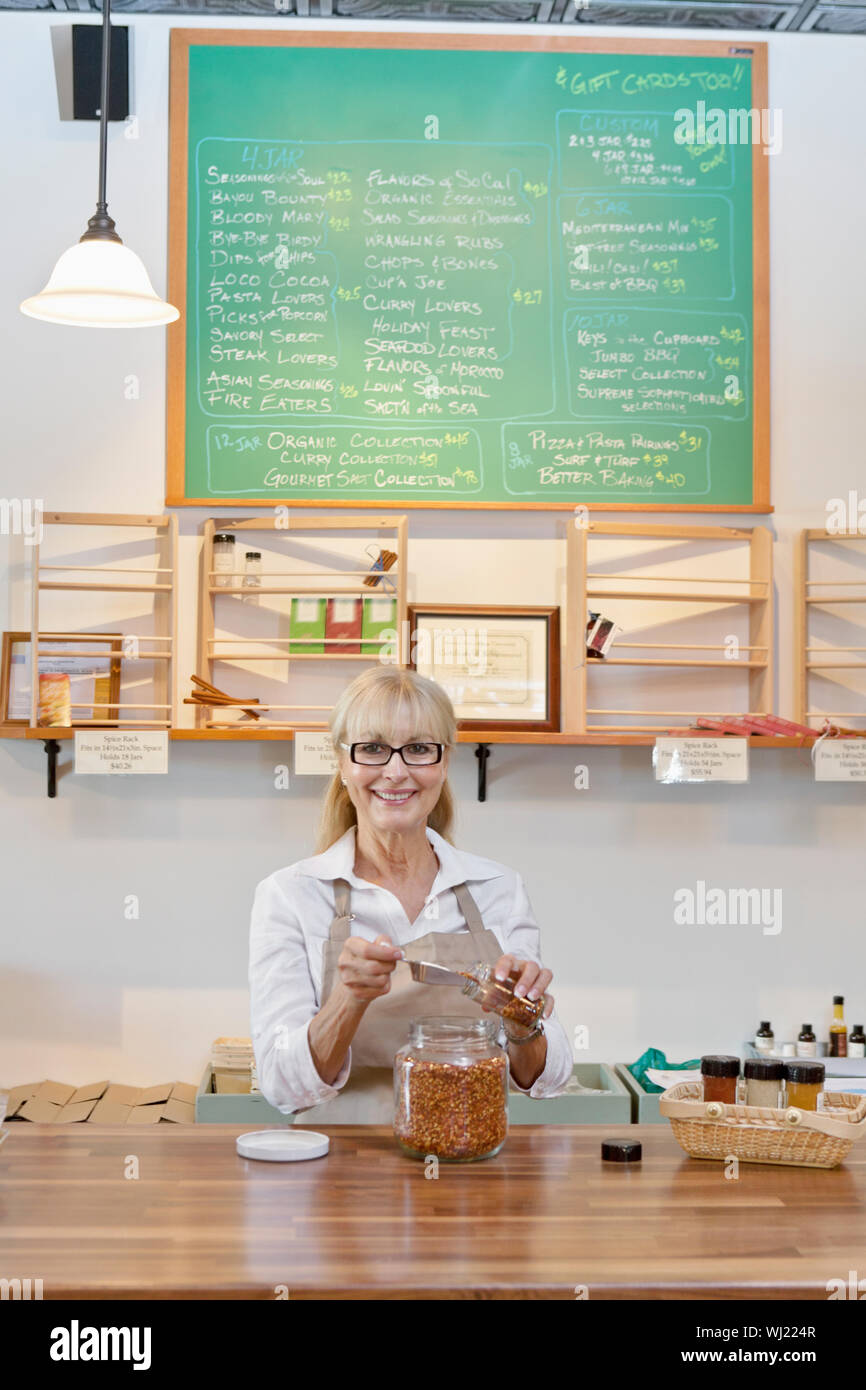Portrait of a happy senior merchant with spice jar at counter in store ...