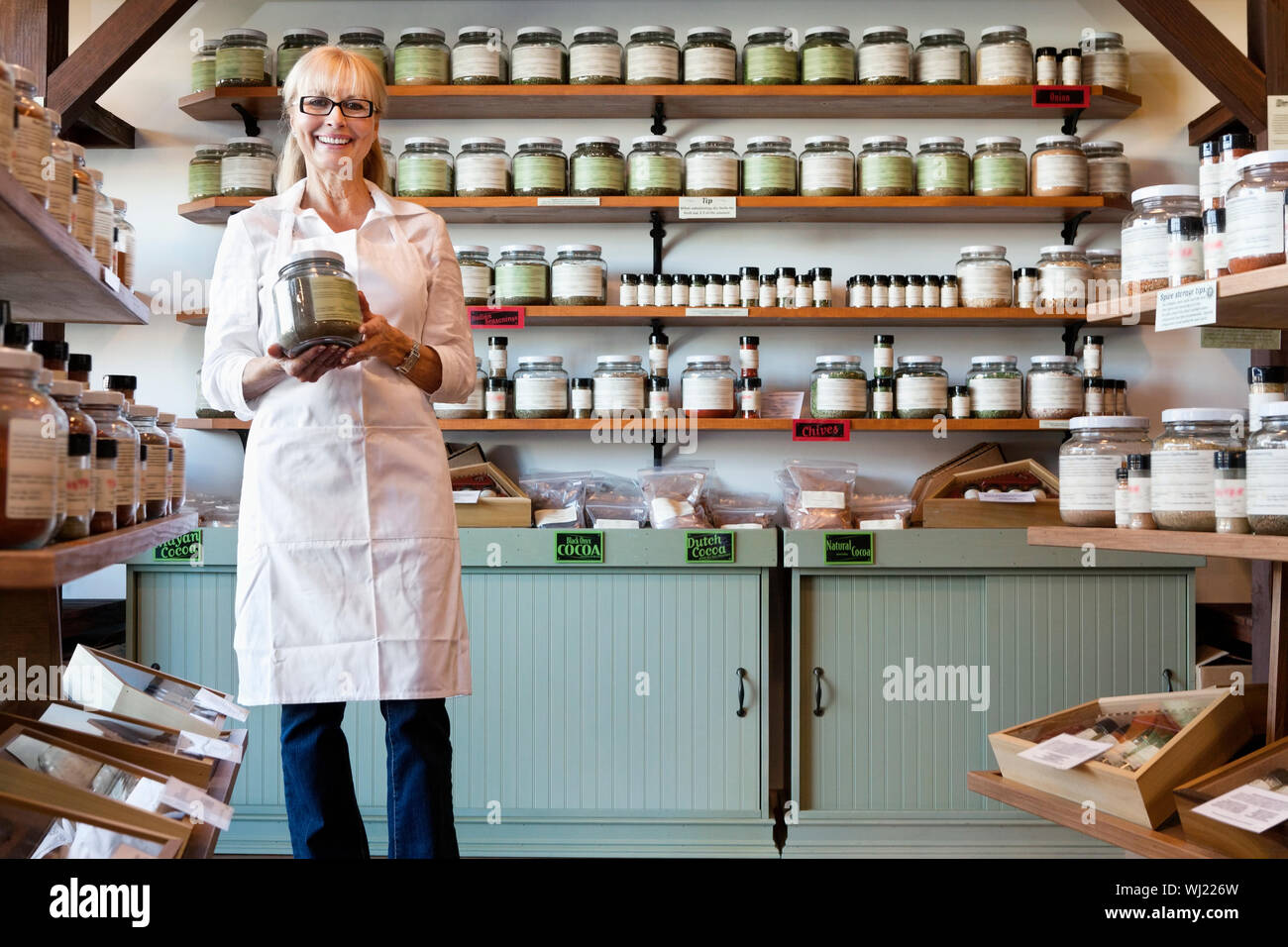 Portrait of a happy senior merchant with spice jar at counter in store ...