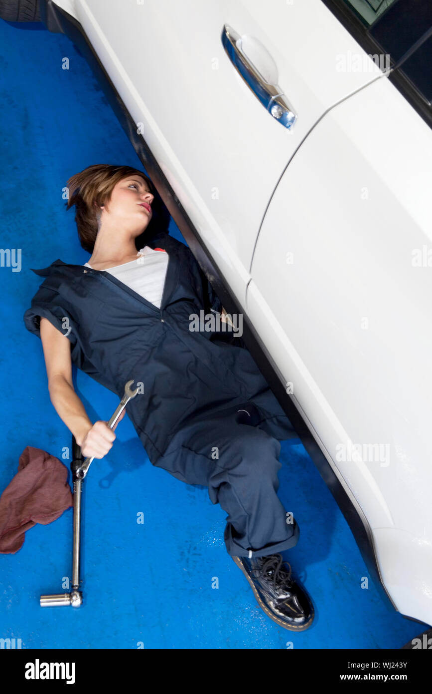 Woman lying down on floor working on car in automobile garage Stock ...