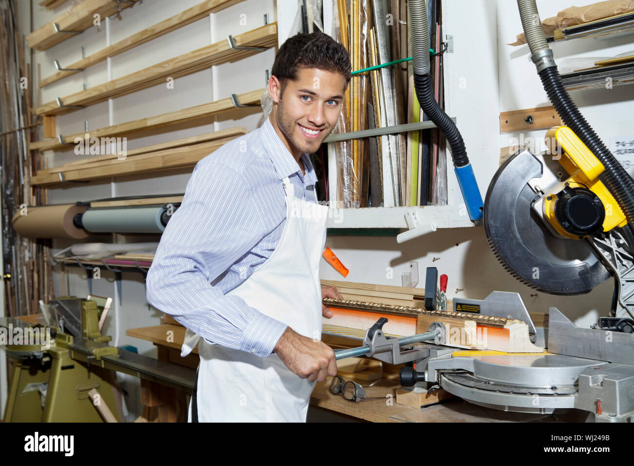 Portrait of a happy young craftsman standing by circular saw machinery ...