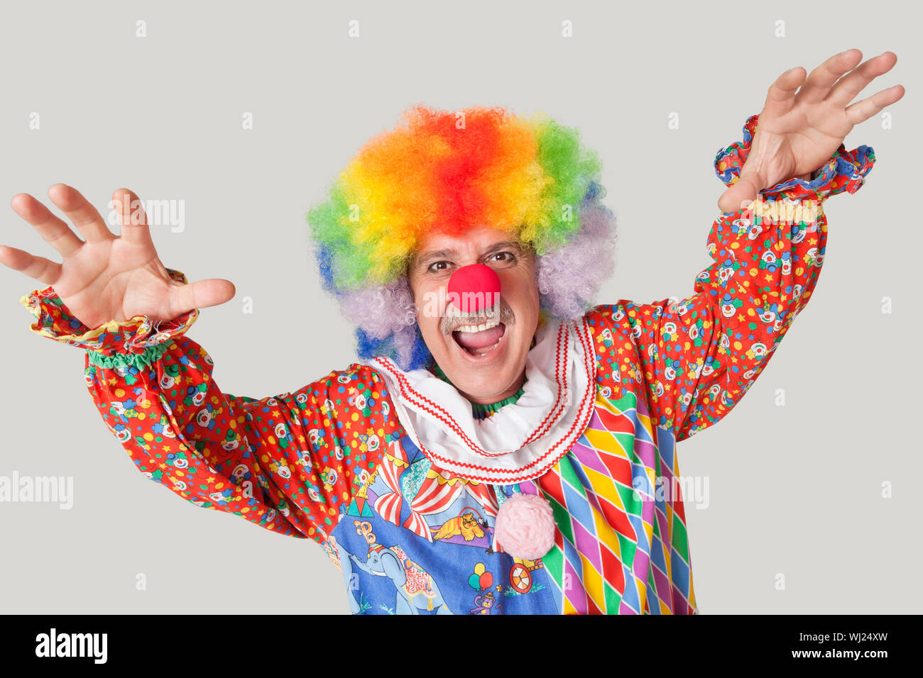 Portrait of funny clown with arms raised and mouth open against colored ...