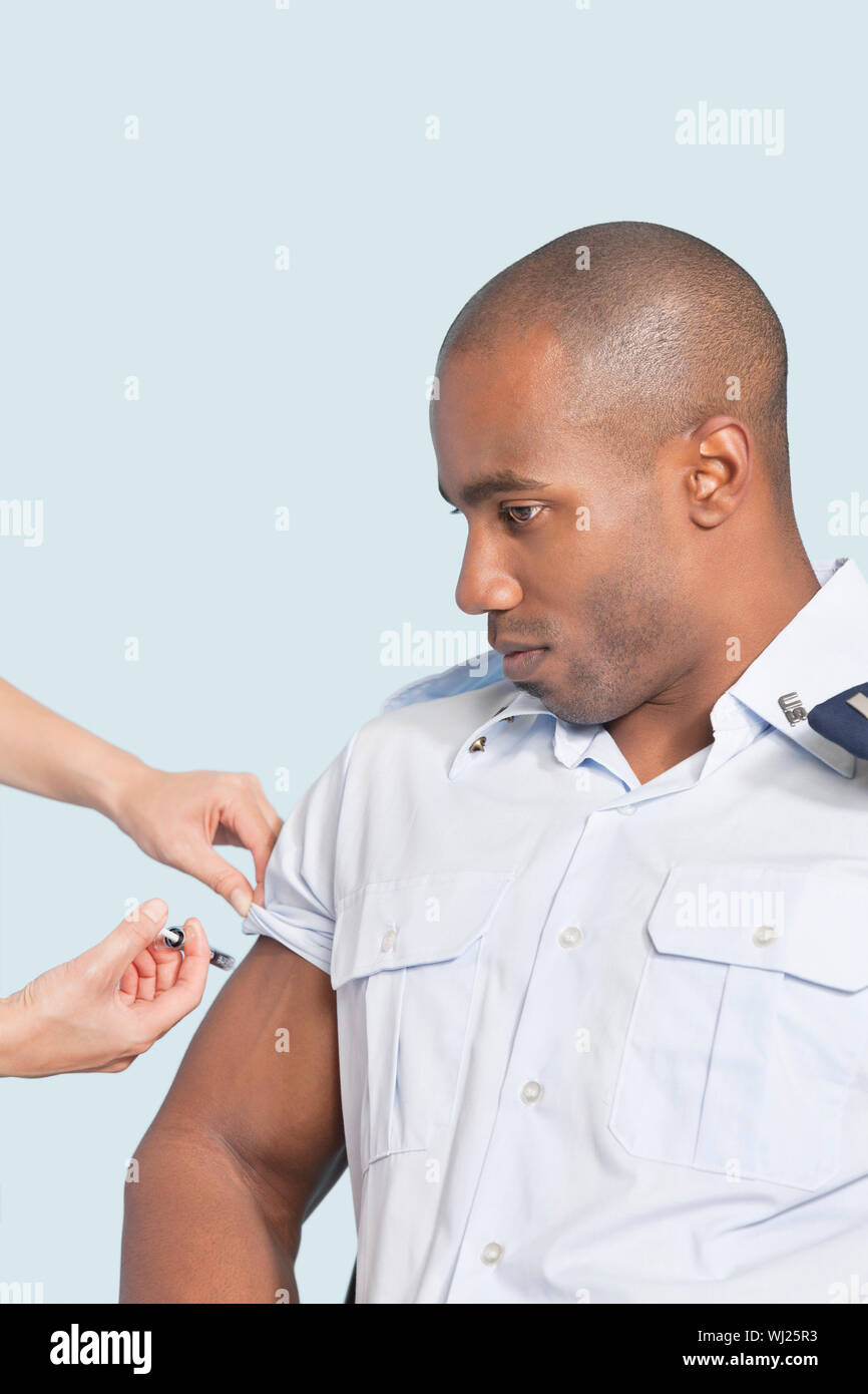Young military man getting an injection from nurse over light blue ...