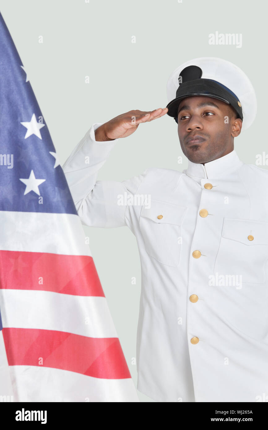 Young Navy officer saluting at American flag against gray background ...